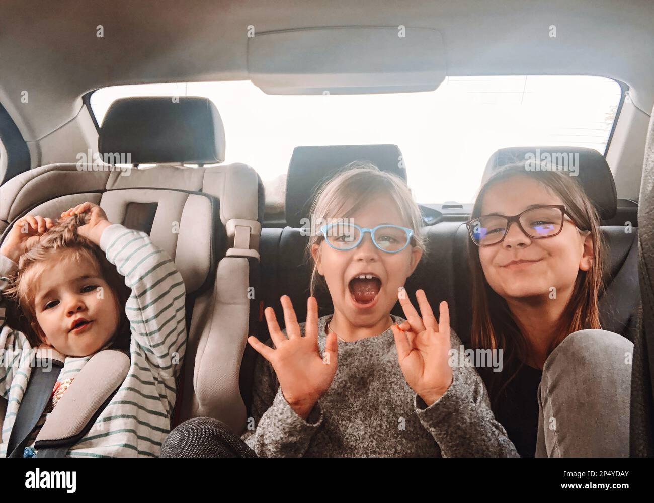 Three cute sisters of different ages are riding in the back seat of a ...