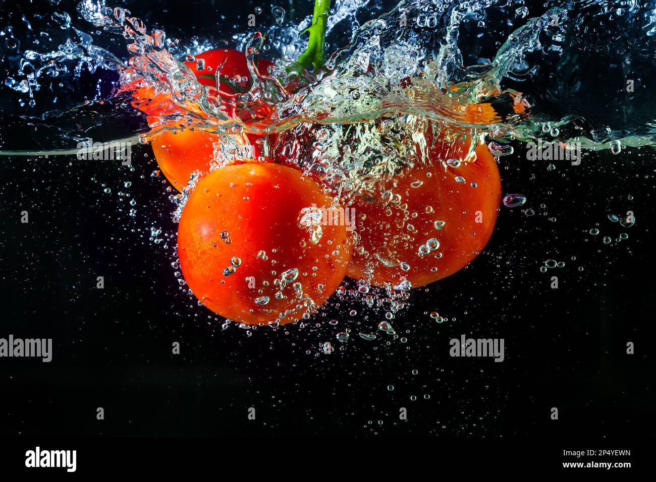 Fresh red tomato falling into water with water splash and air bubbles ...