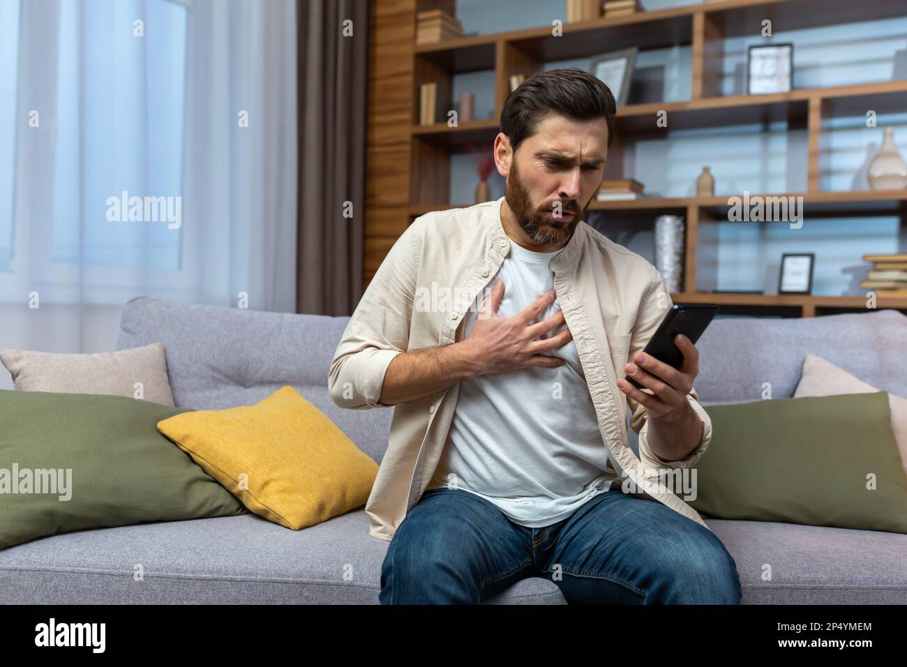 A young man sits at home on the sofa and calls an ambulance, calling a ...