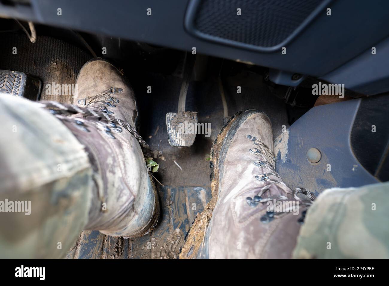 Close-up of a man's legs in military camouflage with trekking boots soiled in mud in the car ...