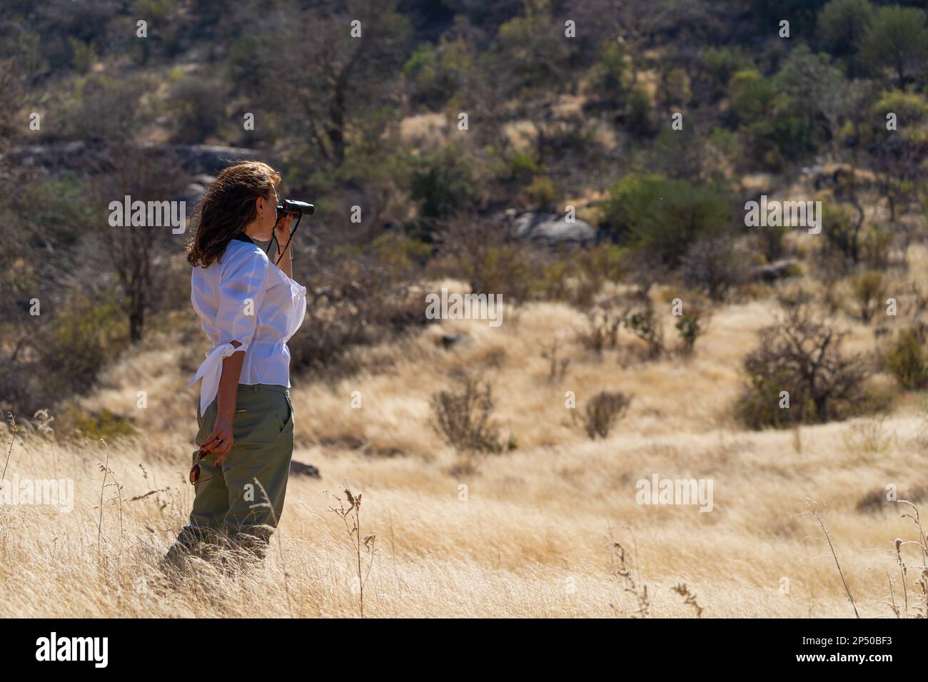 Young female tourist standing outside and watching samburu wildlife with binoculars in kenya ...