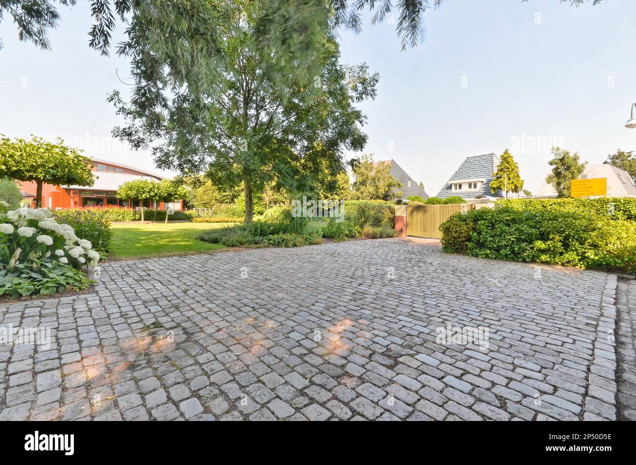a brick paved driveway with trees and bushes in the fore - image taken ...