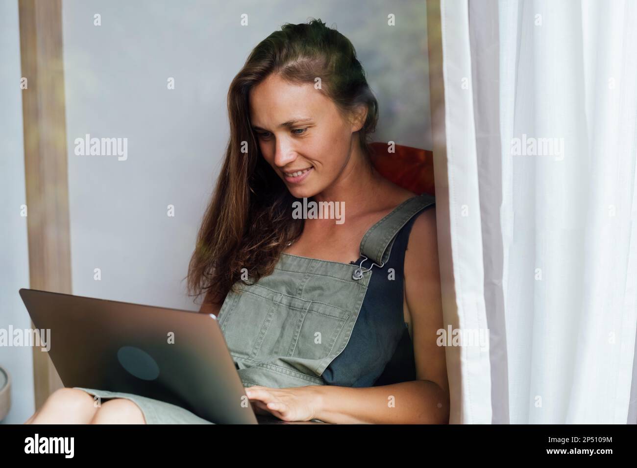 View through a glass window on woman sitting on windowsill and using ...