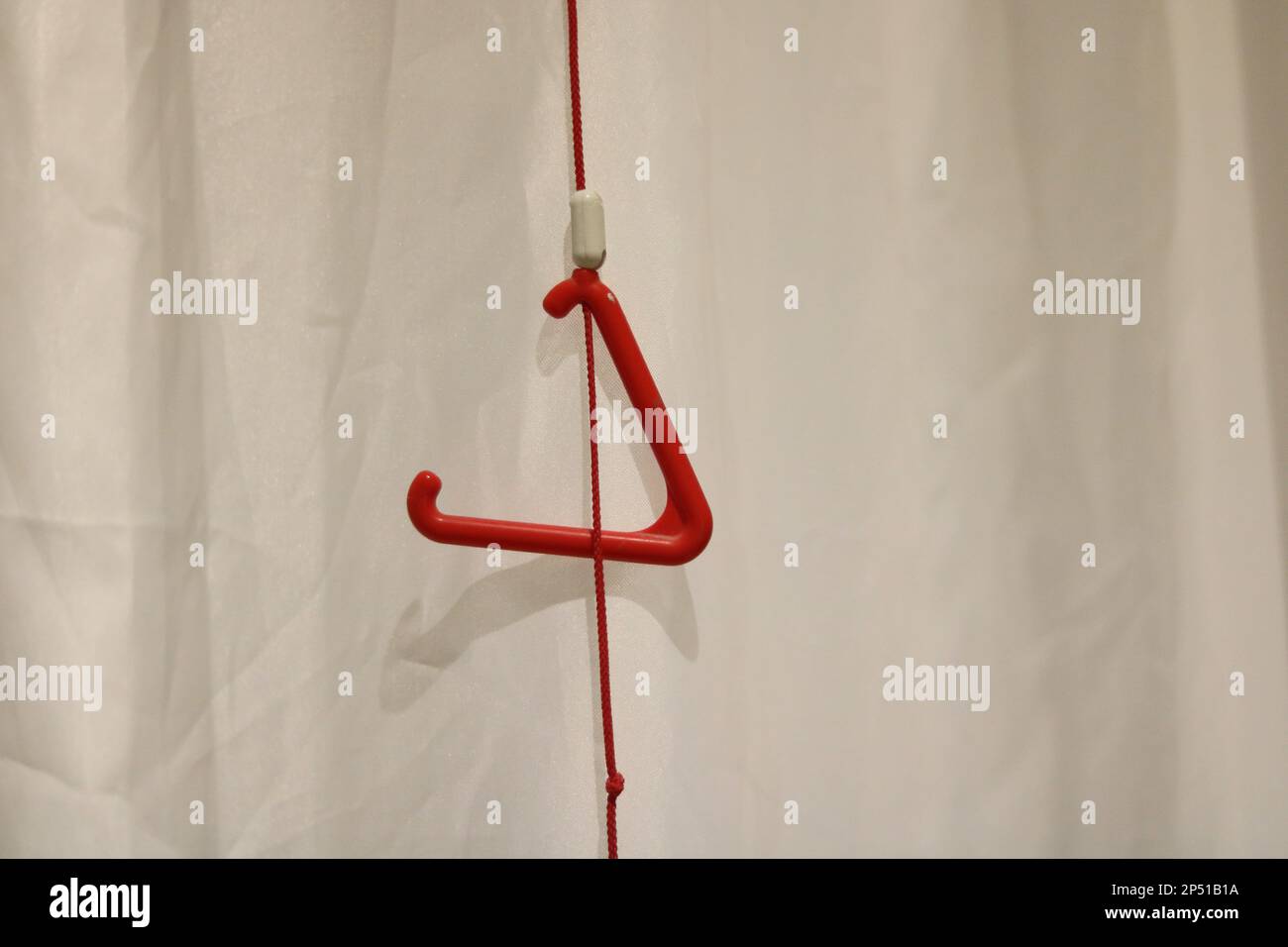 Triangular red emergency pull cord against neutral background with copy ...