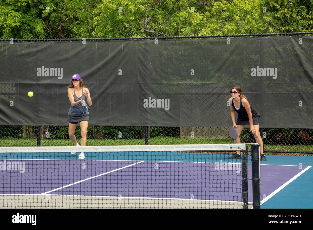 A pickleball player serves while her partner prepares for a return on a ...