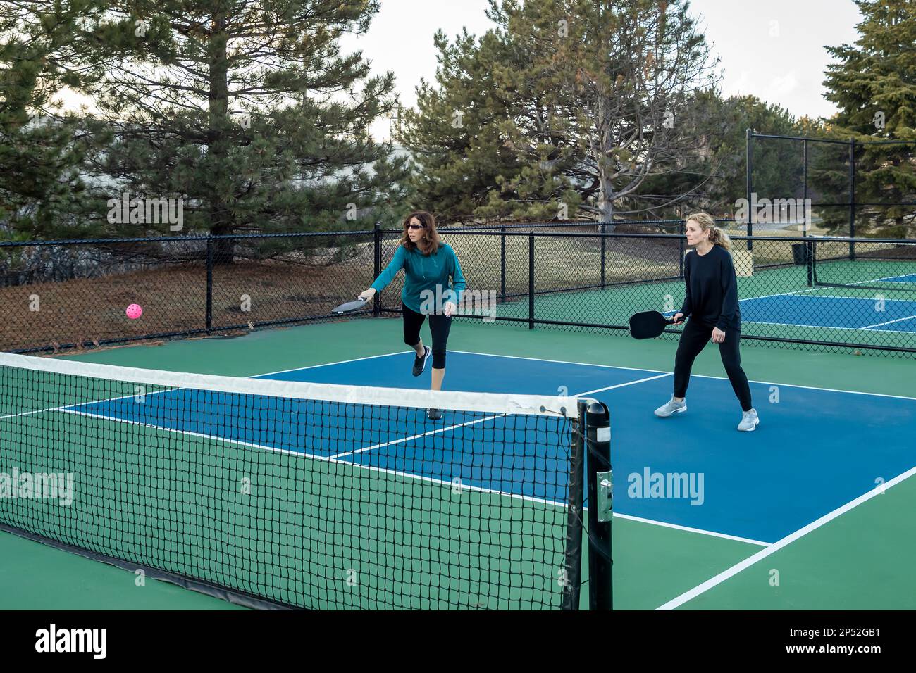 A female pickleball player returns a volley on a blue and green court ...