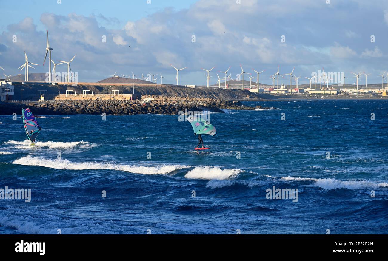 Windsurfers, one with hydrofoil, wind turbines behind at sea off the ...