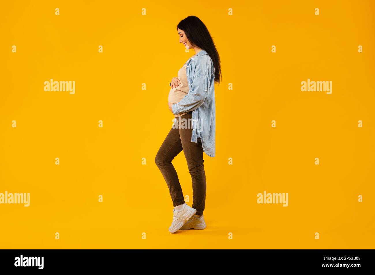 Young expecting lady touching, looking at her belly and smiling ...