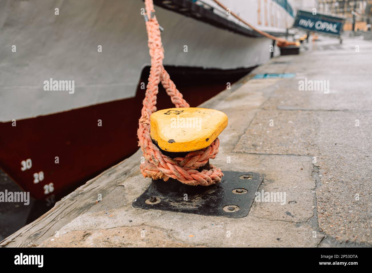 yellow metal mooring post with a black knotted rope in front of the ...