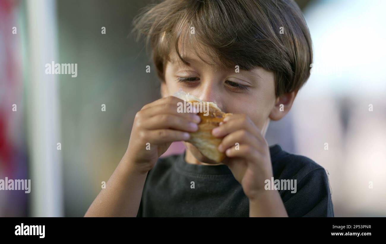 Portrait of child eating piece of bread croissant. Close up face of one ...
