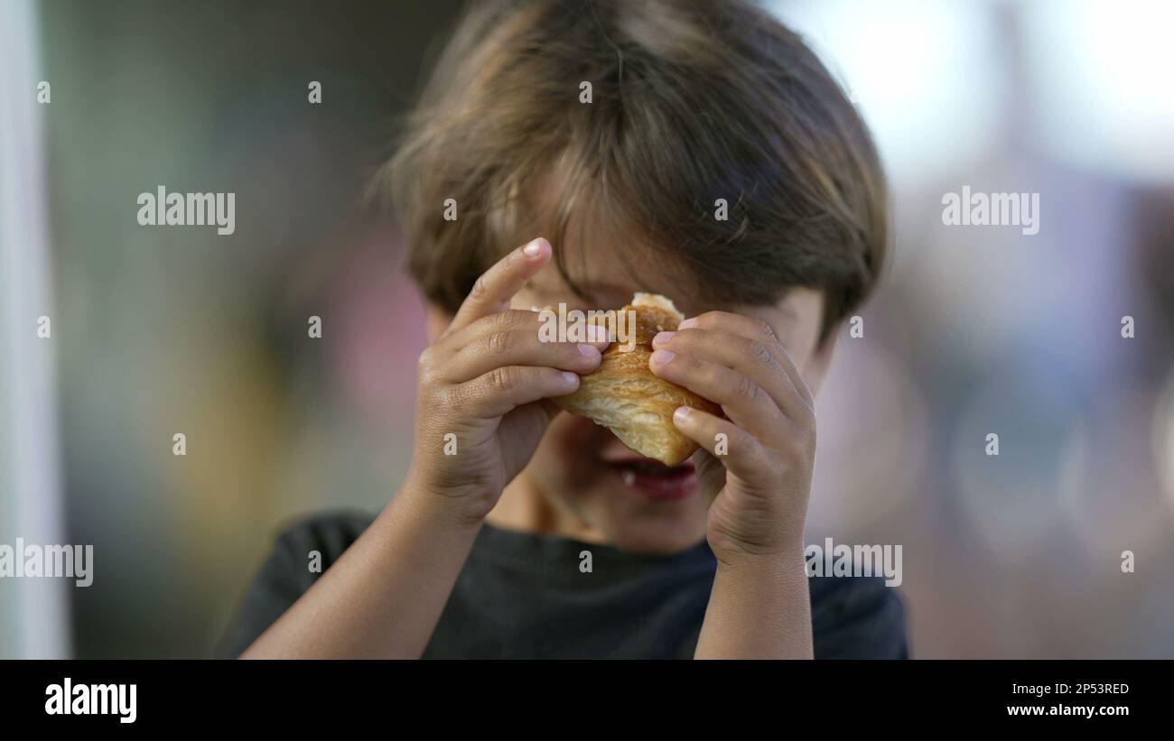 Portrait of child eating piece of bread croissant. Close up face of one ...