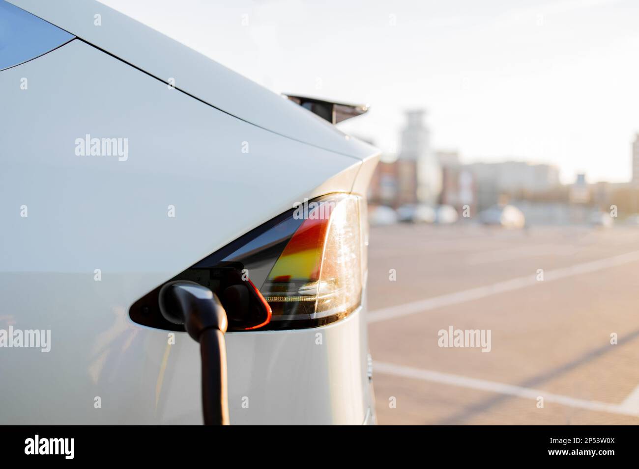 White luxury electric car with plug cord connected to charging port at ...