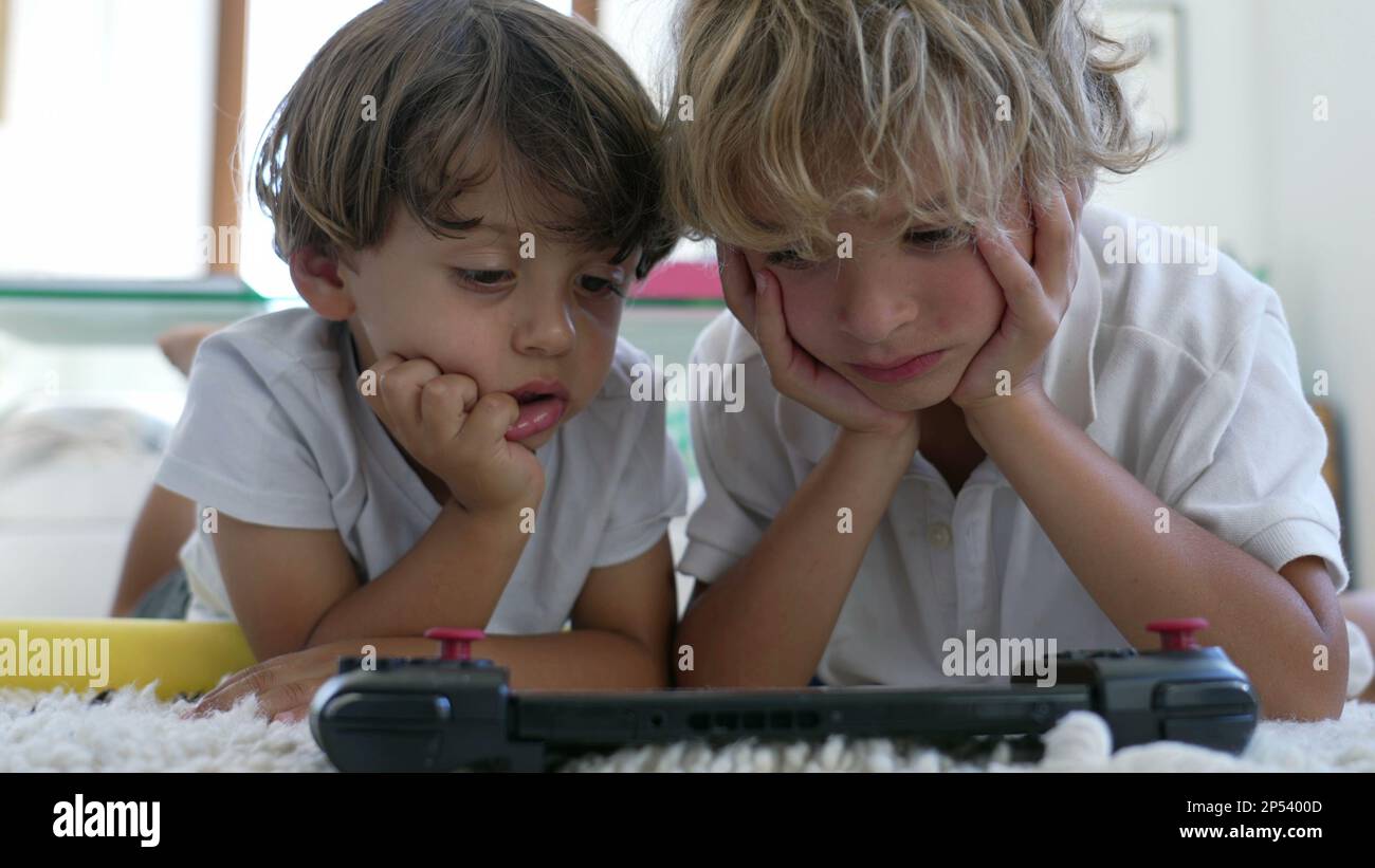 Two small boy with hand in chin watching media online with tablet ...