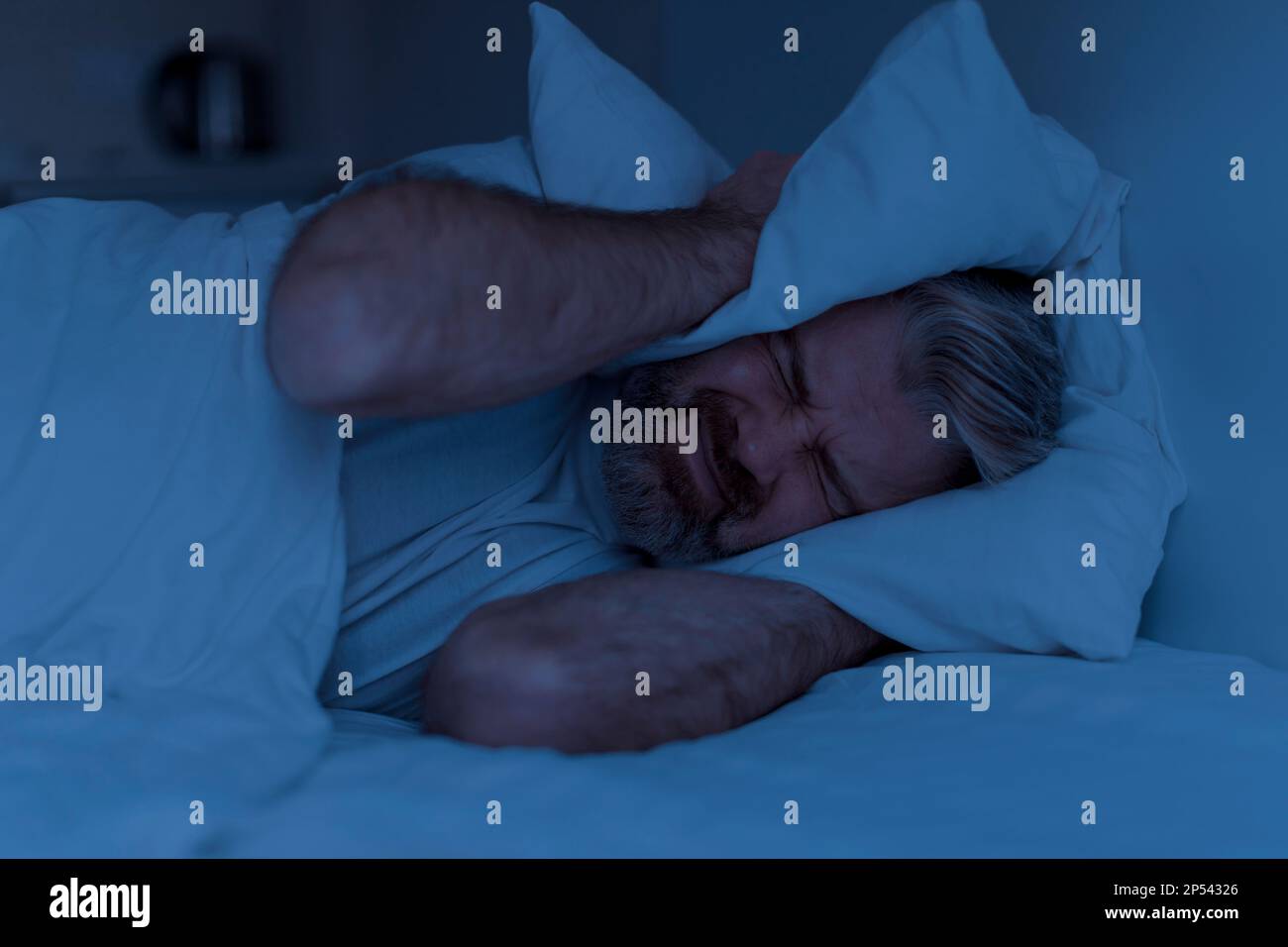 Closeup of angry mature man covering head with pillow Stock Photo - Alamy