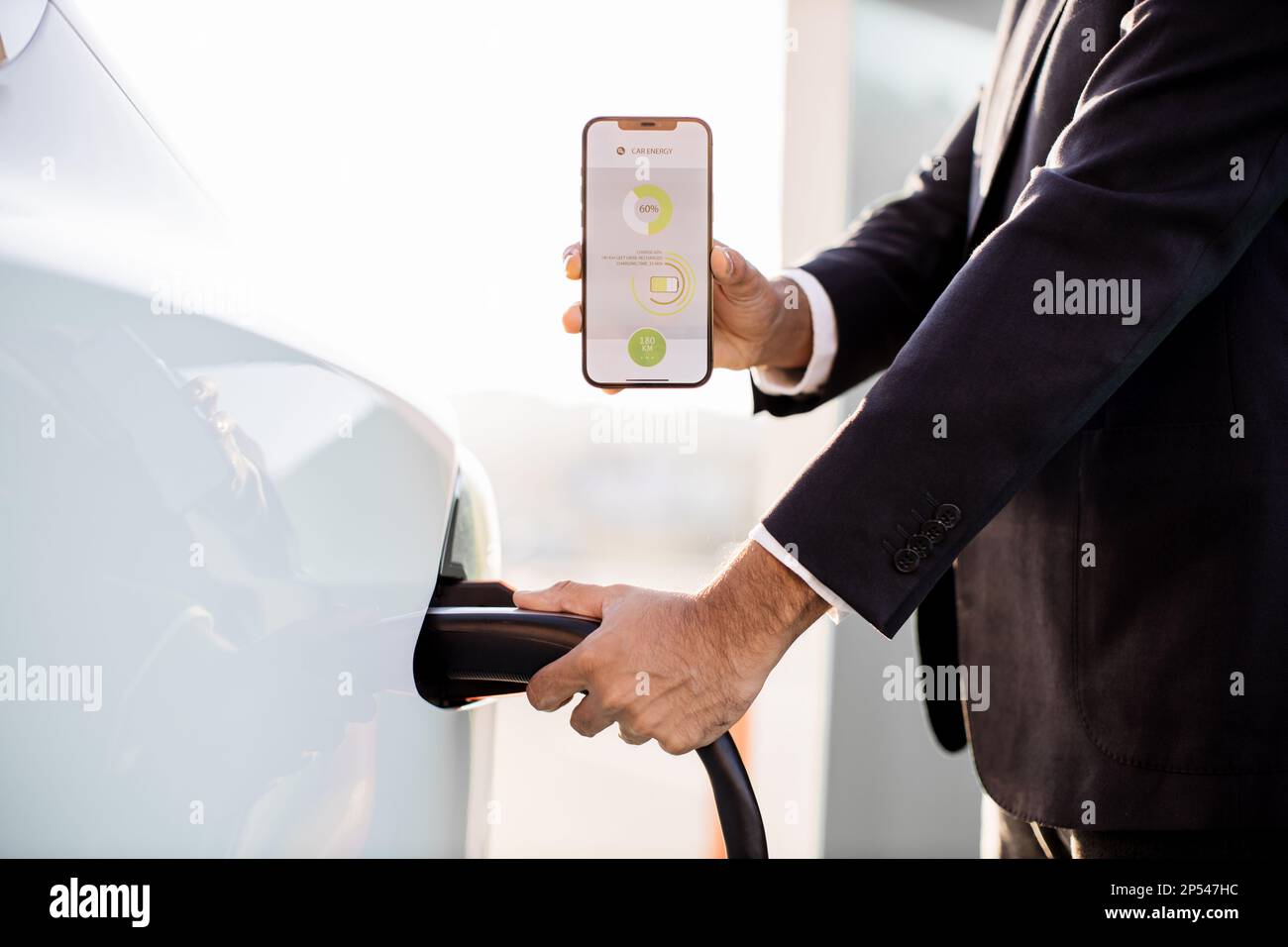 Crop of man in black suit plugging power cord and showing mobile screen ...