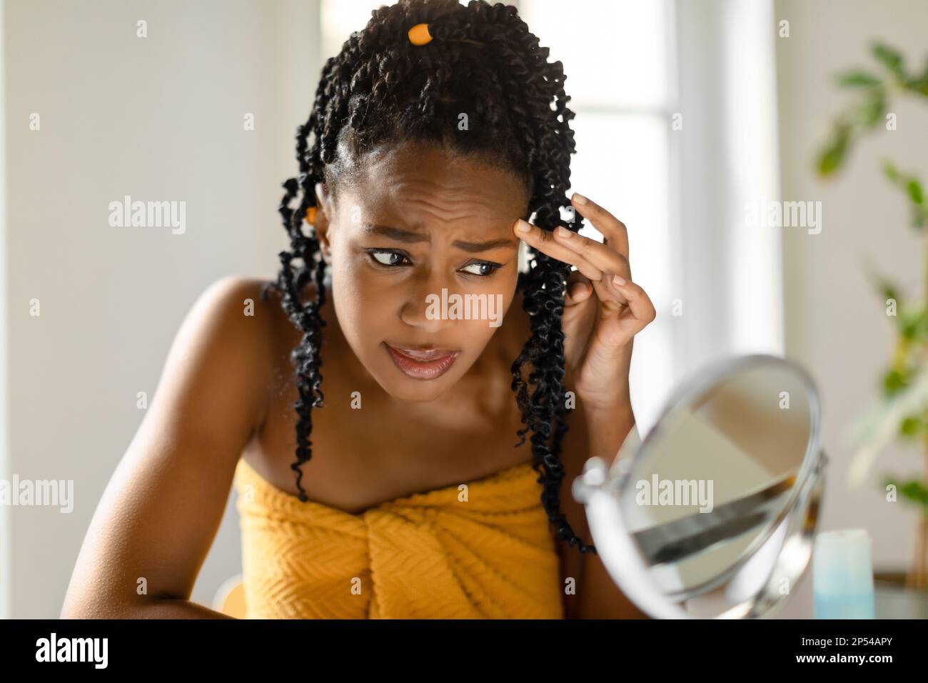 Upset black lady looking at mirror, checking her wrinkles on foreheads ...