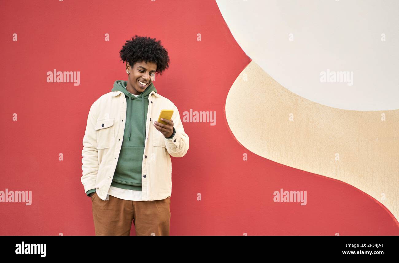 Smiling African American gen z teenager standing at color wall using ...