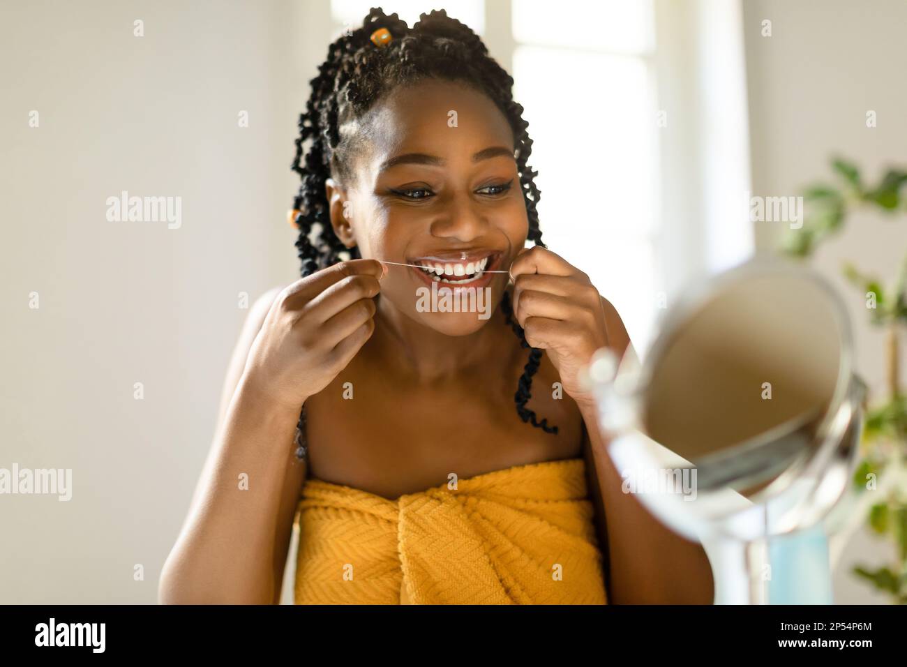 Attractive black woman looking at mirror and using dental floss ...