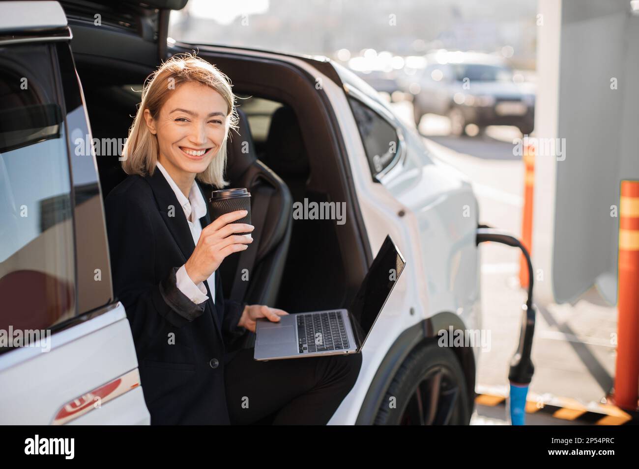 Charming young lady in business suit working on laptop and drinking ...