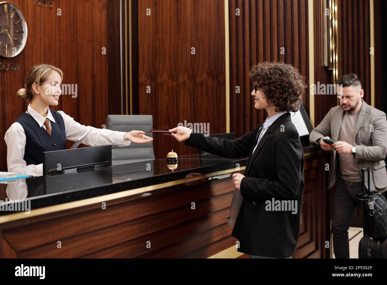 Happy young female receptionist in uniform taking passport of hotel ...