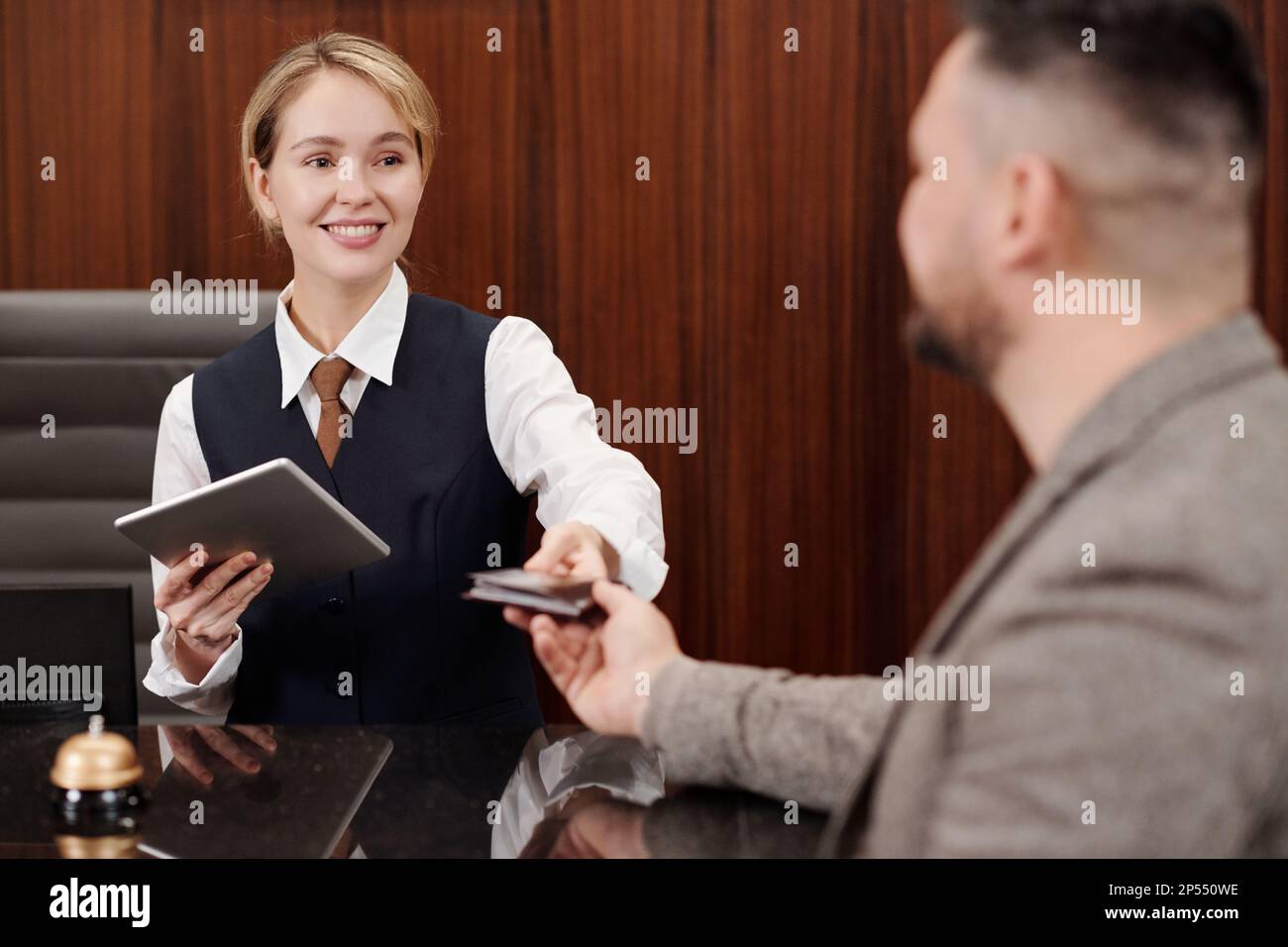 Young smiling receptionist giving passport back to male guest over ...