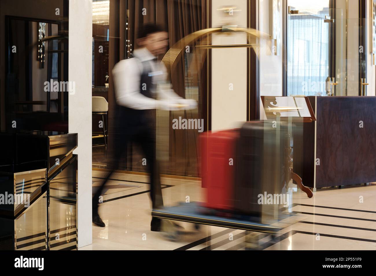 Blurry motion of bellboy walking fast along lounge or hall of luxurious ...