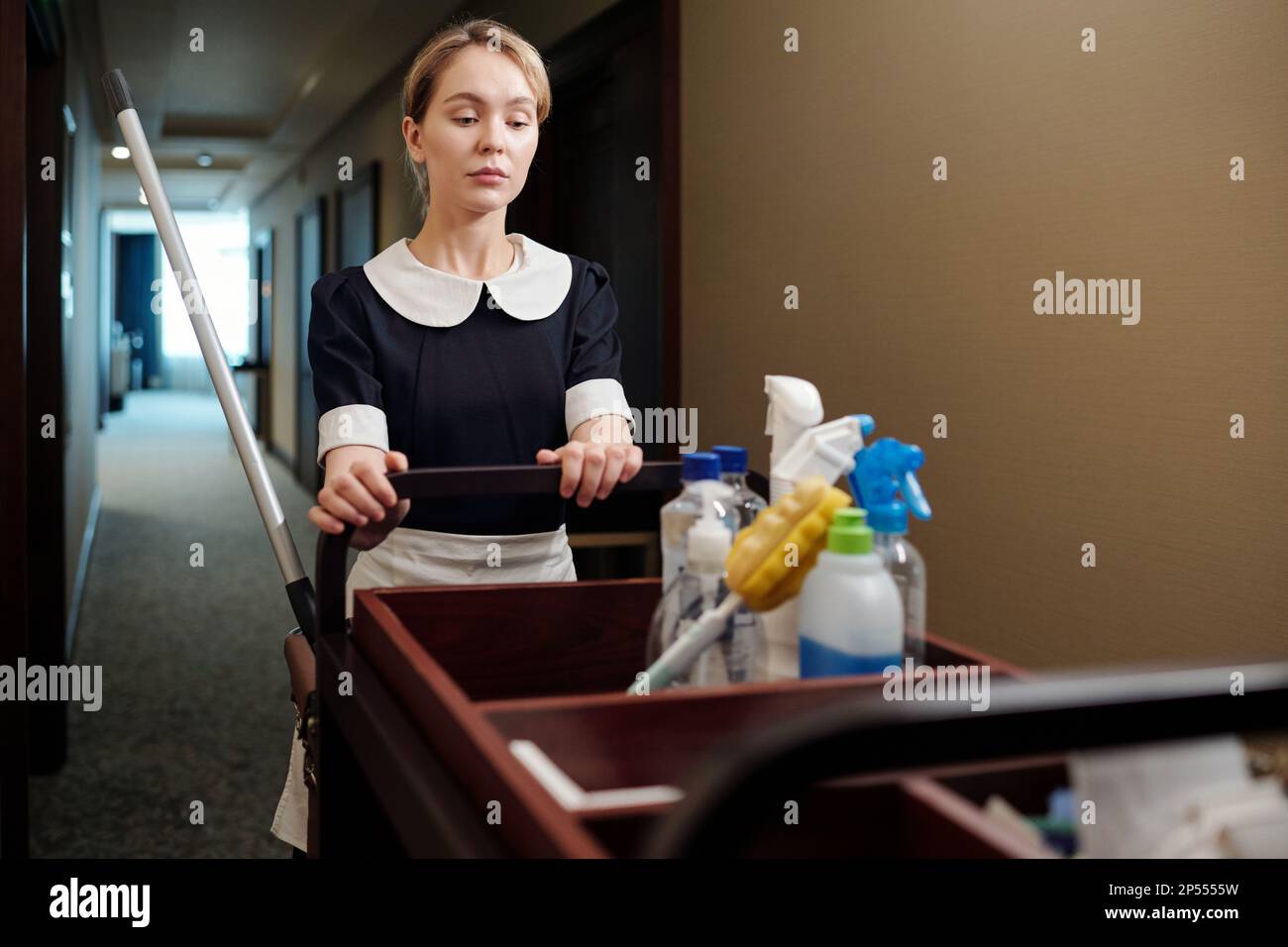 Young blond chambermaid with cart full of detergents walking round ...