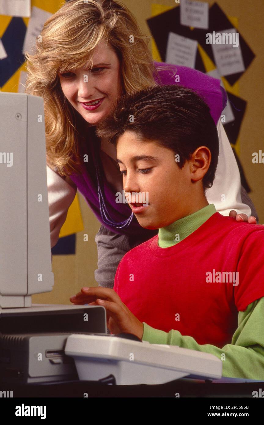 Young male student working at a computer while female teacher looks ...