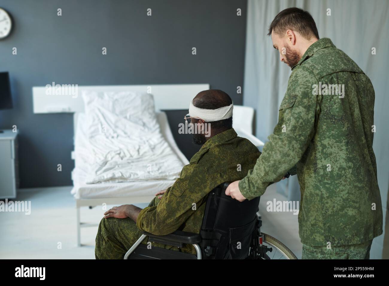Young soldier in camouflage pushing wheelchair with his friend while ...