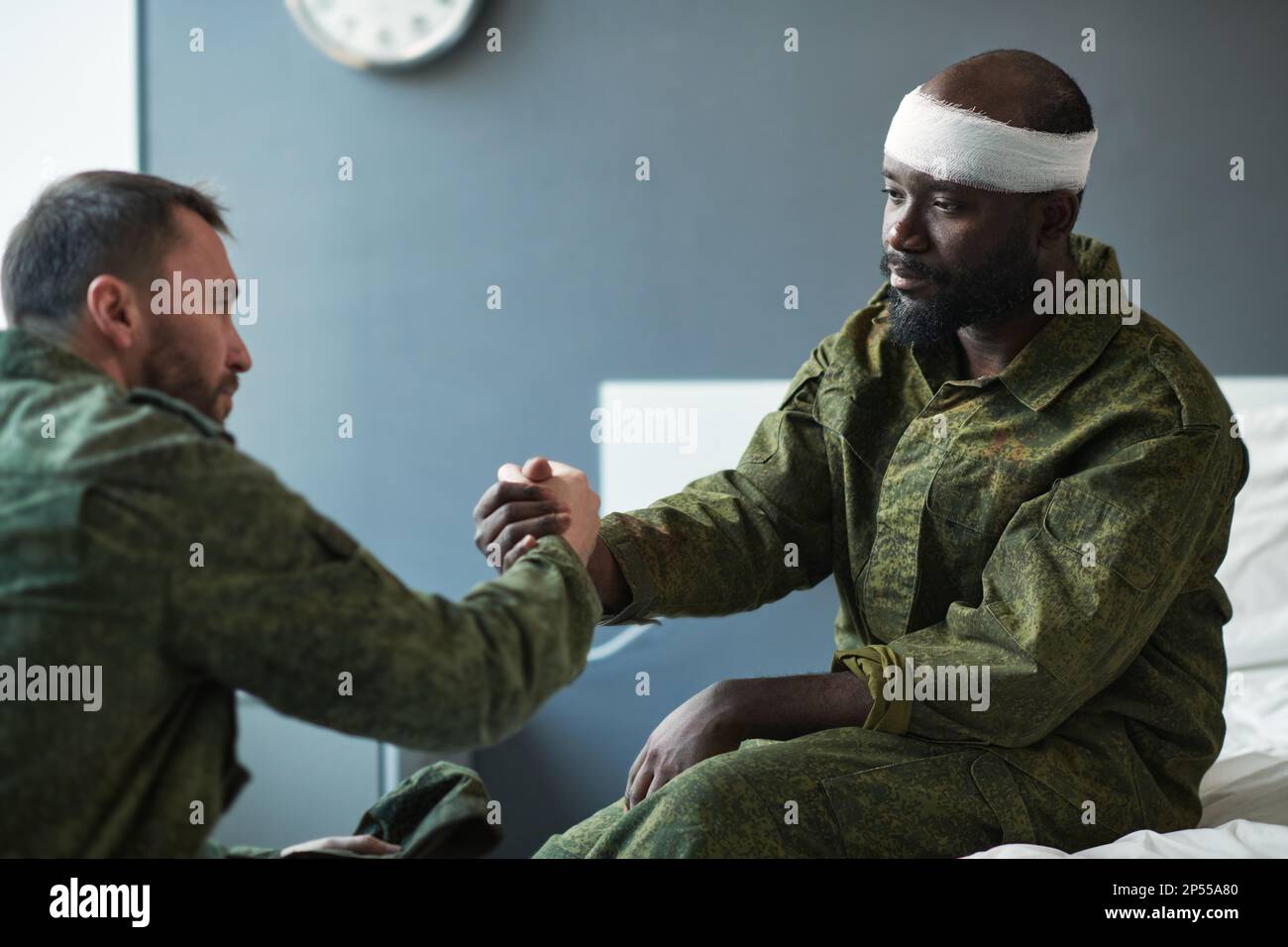 Young soldier shaking hand of African American friend with injured head ...