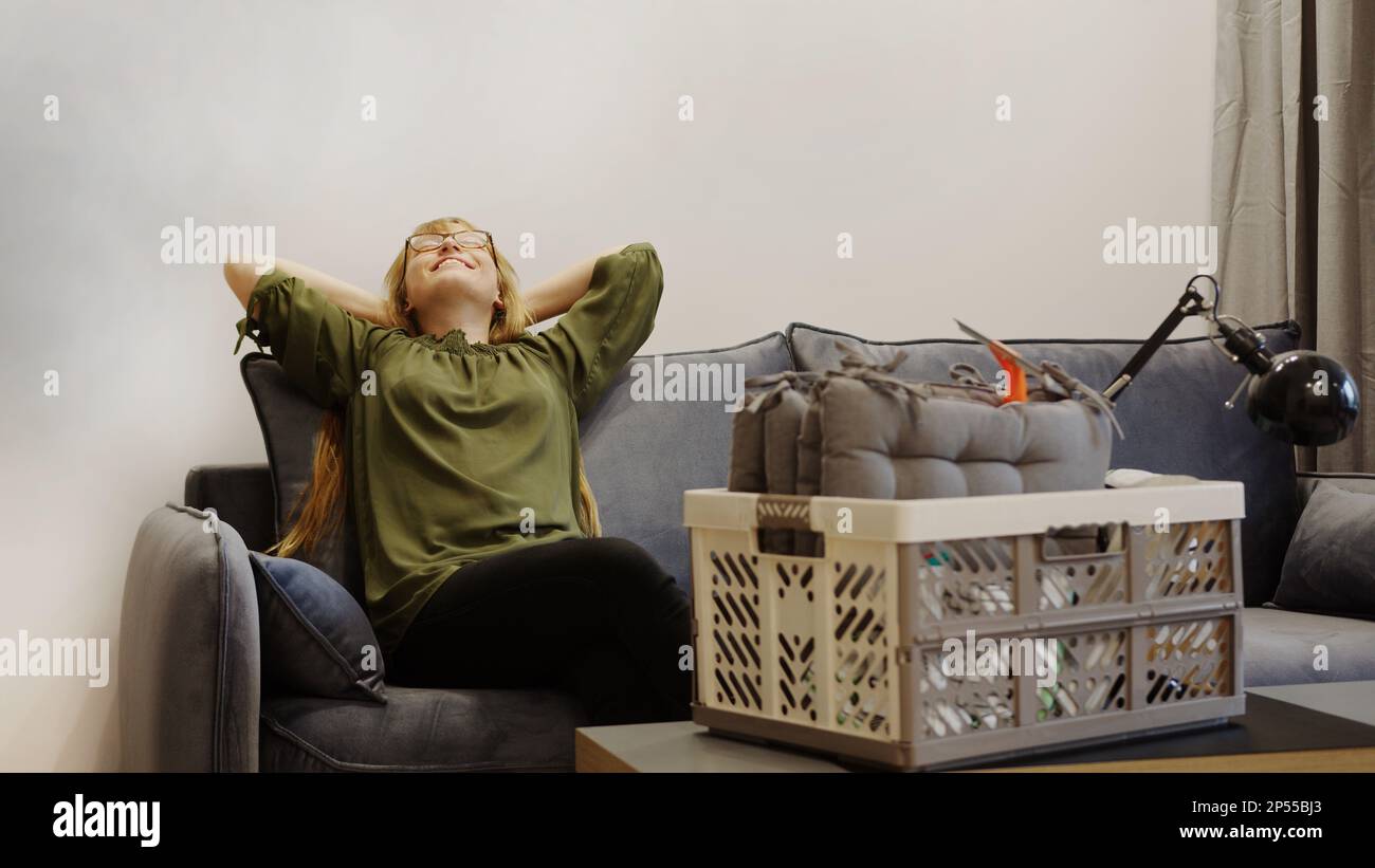 happy woman resting on the couch after moving in and a box on the table ...