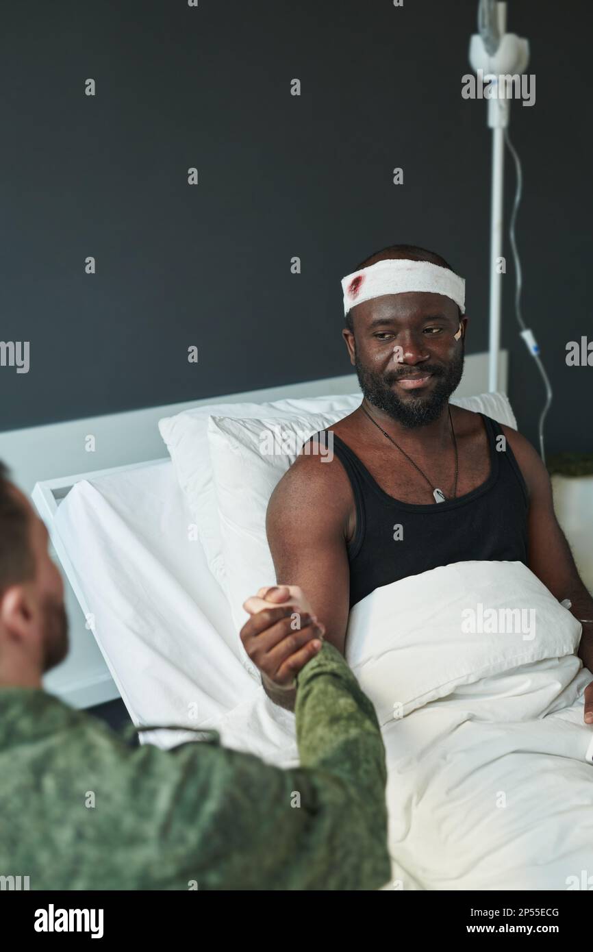 Young injured soldier with bandaged head sitting on bed in ward of ...