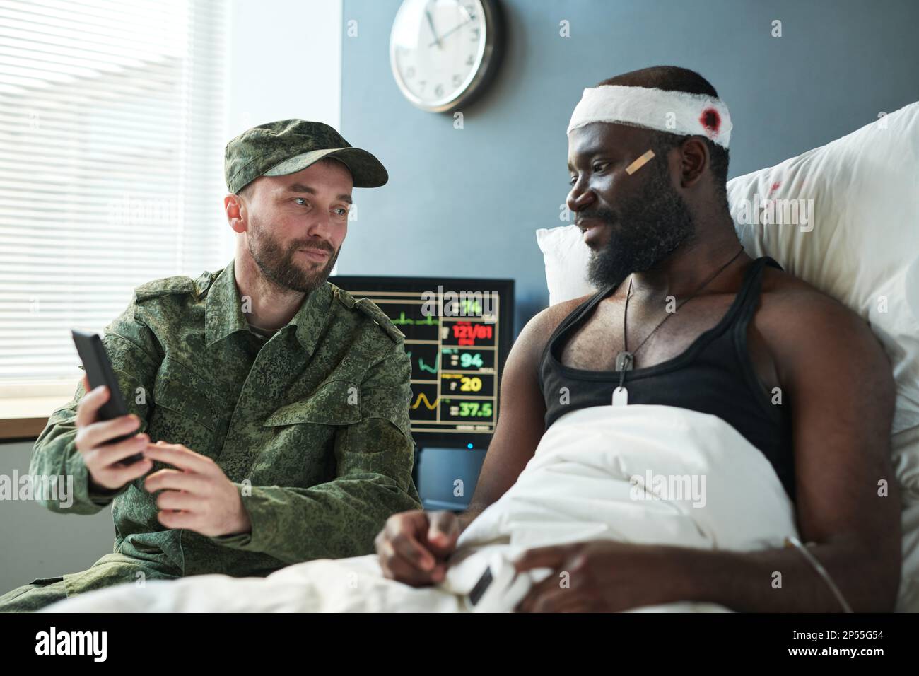 Happy soldier with injured head looking at screen of smartphone held by ...