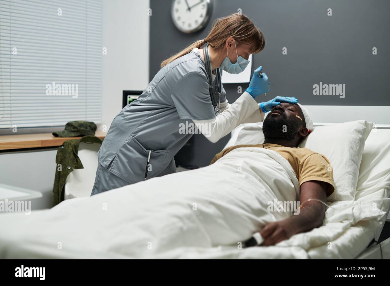 Nurse with special medical device directing light on eyes of injured ...