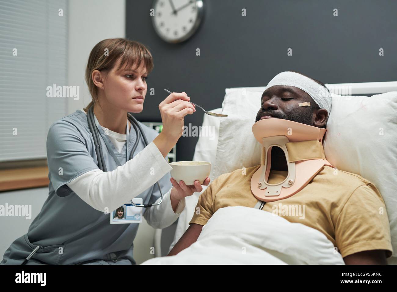 Nurse in uniform holding bowl with porridge while feeding injured ...