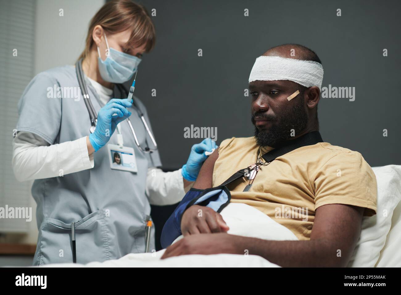 Young injured man with bandaged head and broken arm sitting in bed ...