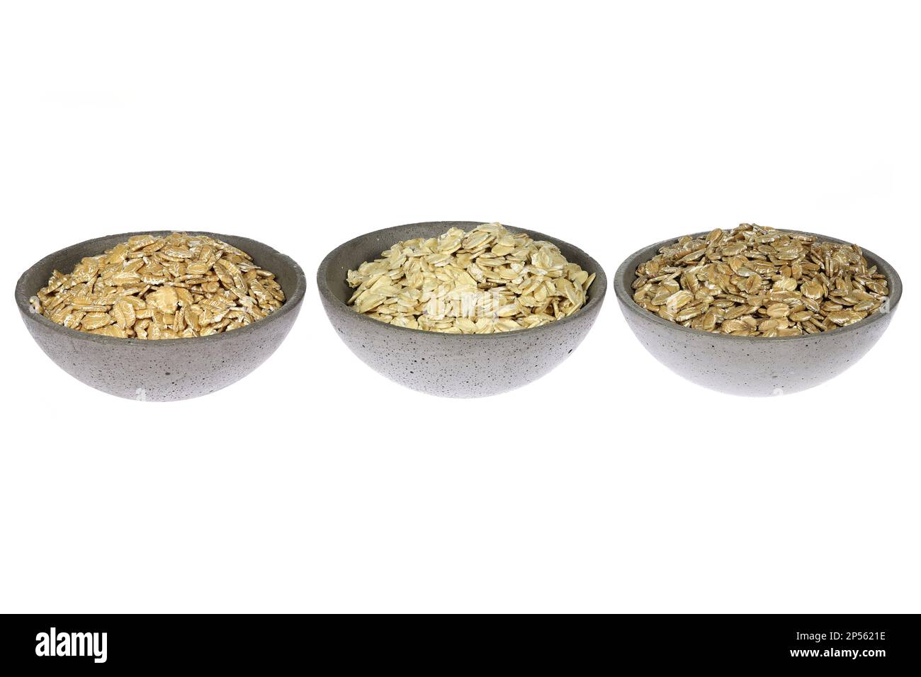 cereal flakes (spelt, oat, rye) in concrete bowls isolated on white ...