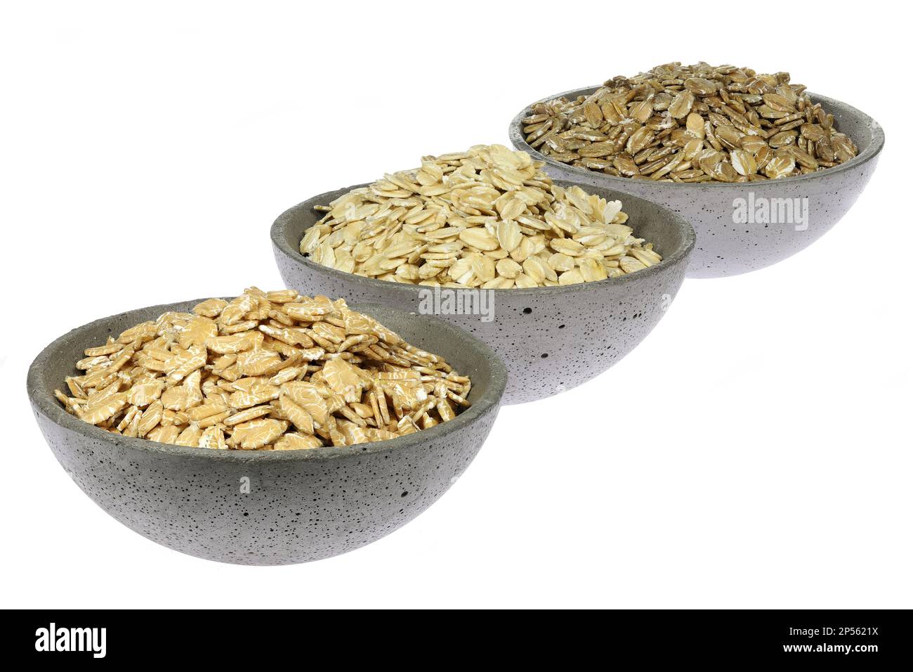 cereal flakes (spelt, oat, rye) in concrete bowls isolated on white ...