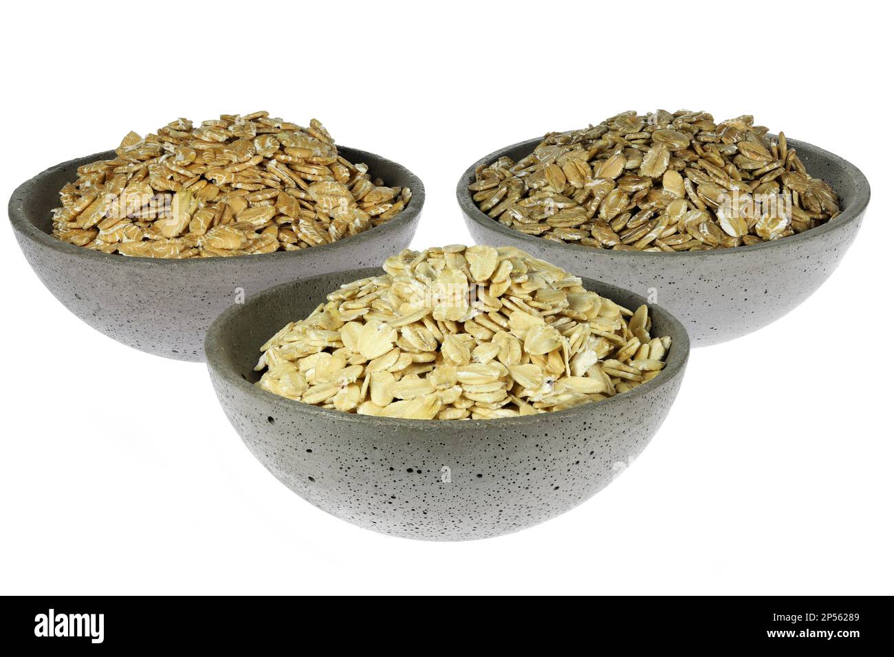 cereal flakes (spelt, oat, rye) in concrete bowls isolated on white ...
