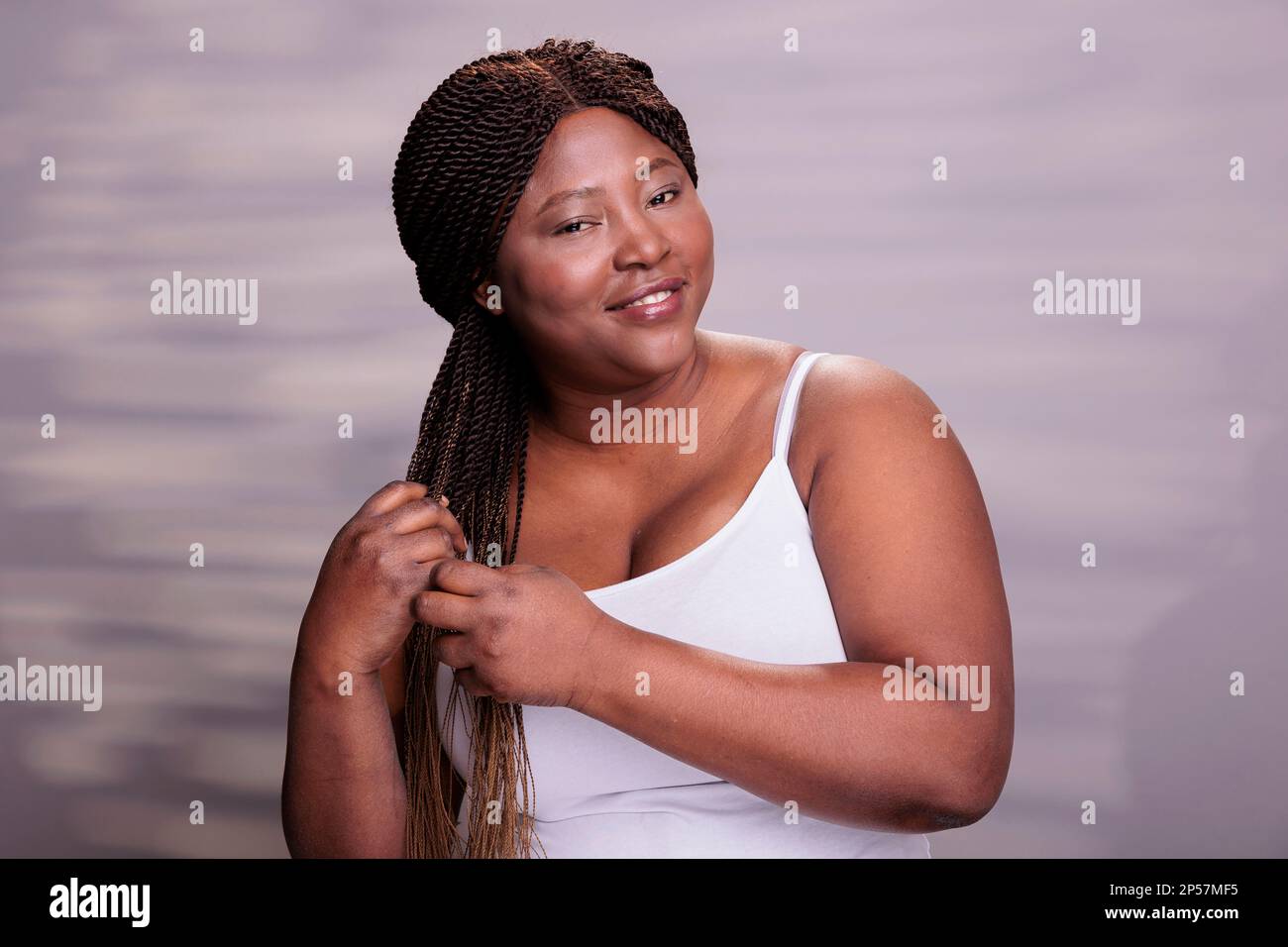 Curvy happy lady making african braids hairstyle and looking at camera ...