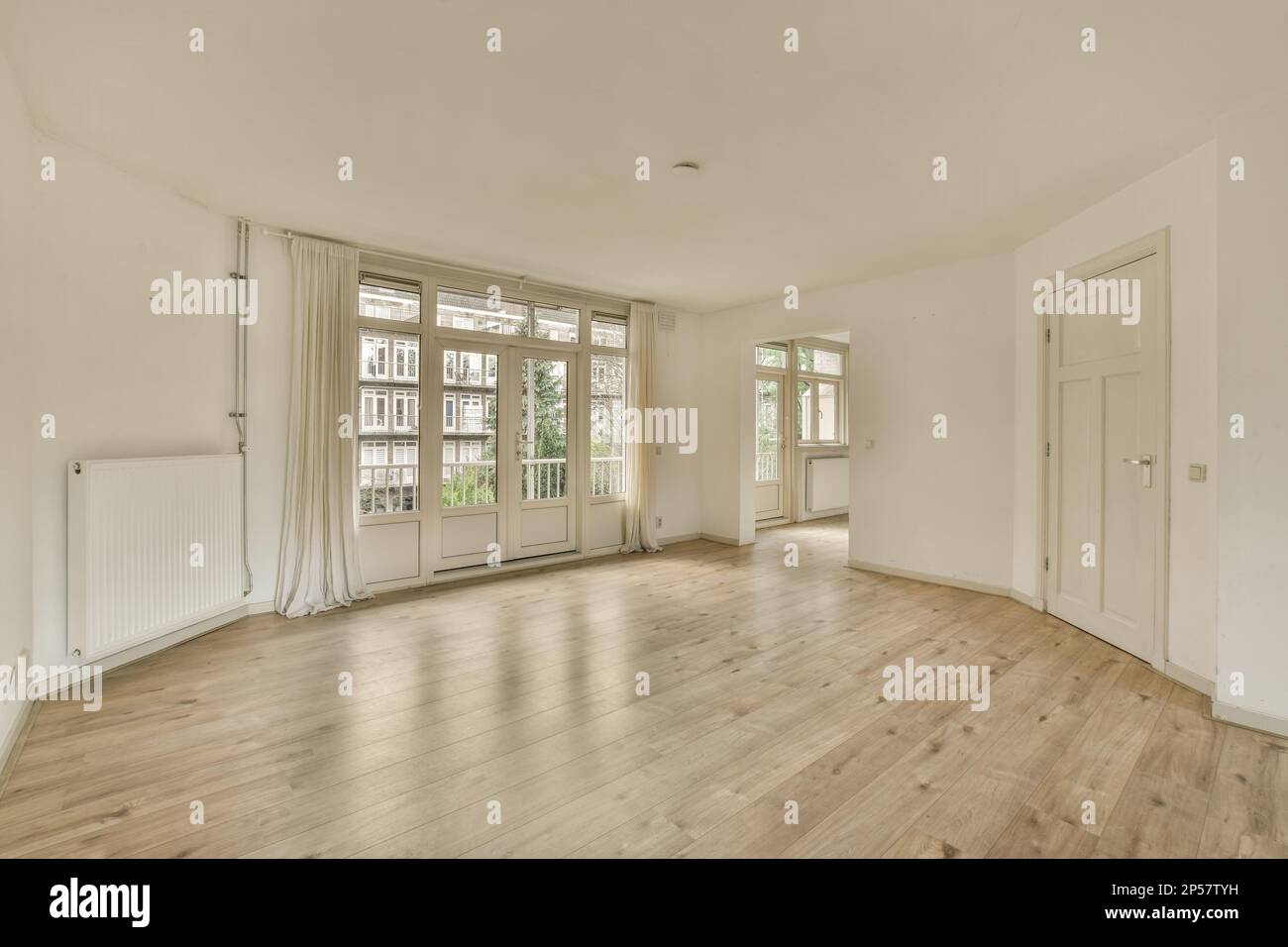 an empty living room with wood flooring and large windows looking out ...
