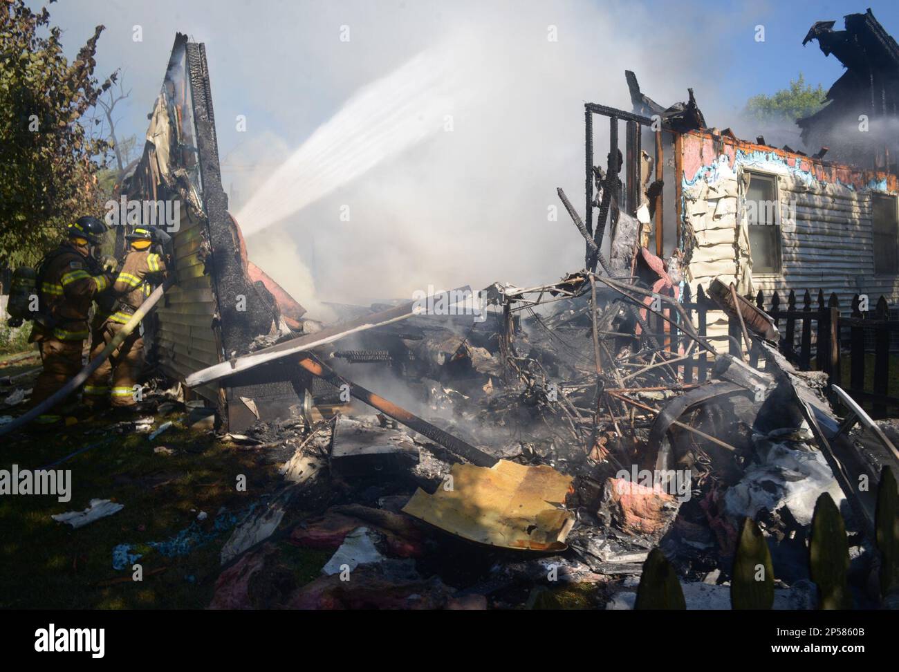 Firefighters pour water into a burned out house, while the skeleton of ...