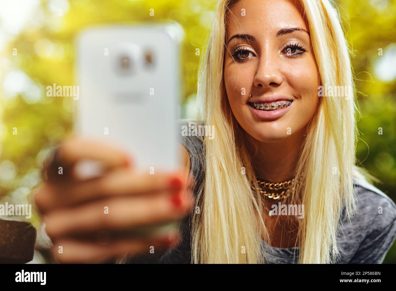 Beautiful blond girl stares amusedly at her own cell phone. Her smile ...