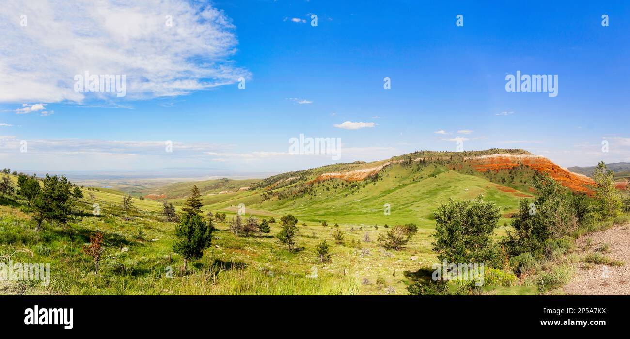 A panorama of green hills and valley textured with layered red rock ...