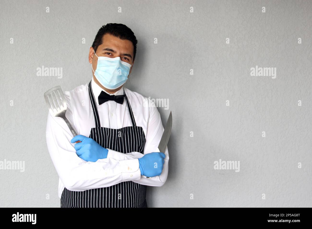 Latino chef with kitchen utensils working with mouth mask and latex ...