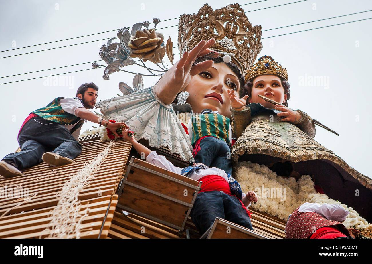 Men placing flower offerings on large wooden replica statue of Virgen ...