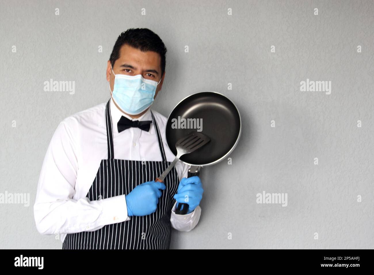 Latino chef with kitchen utensils working with mouth mask and latex ...