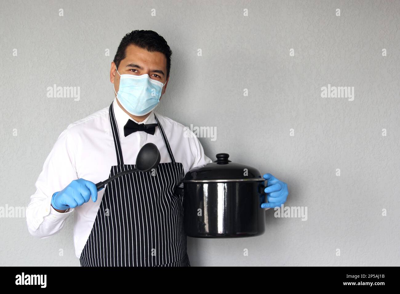 Latino chef with kitchen utensils working with mouth mask and latex ...