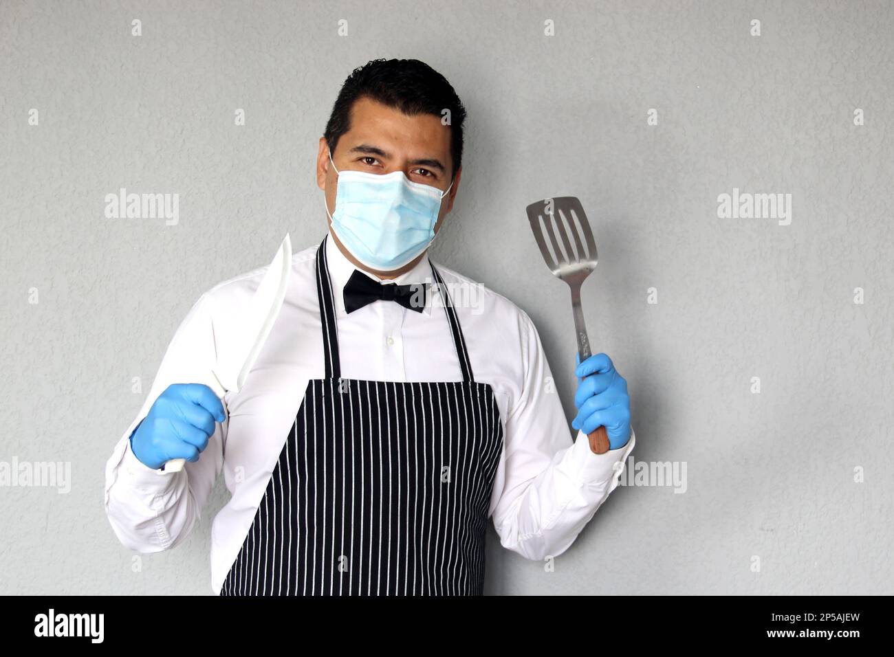 Latino chef with kitchen utensils working with mouth mask and latex ...