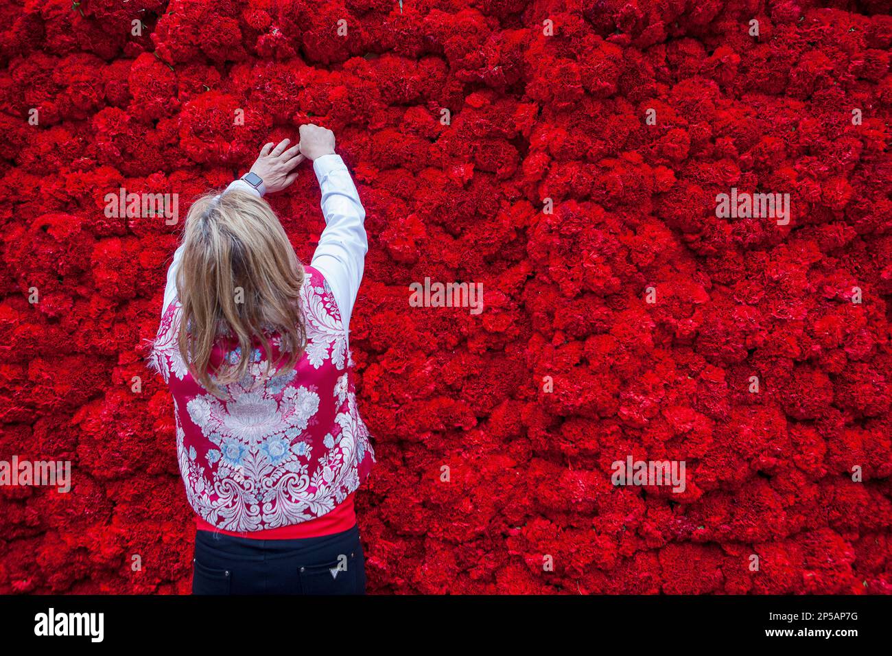 Woman placing flower offerings on large wooden replica statue of Virgen ...